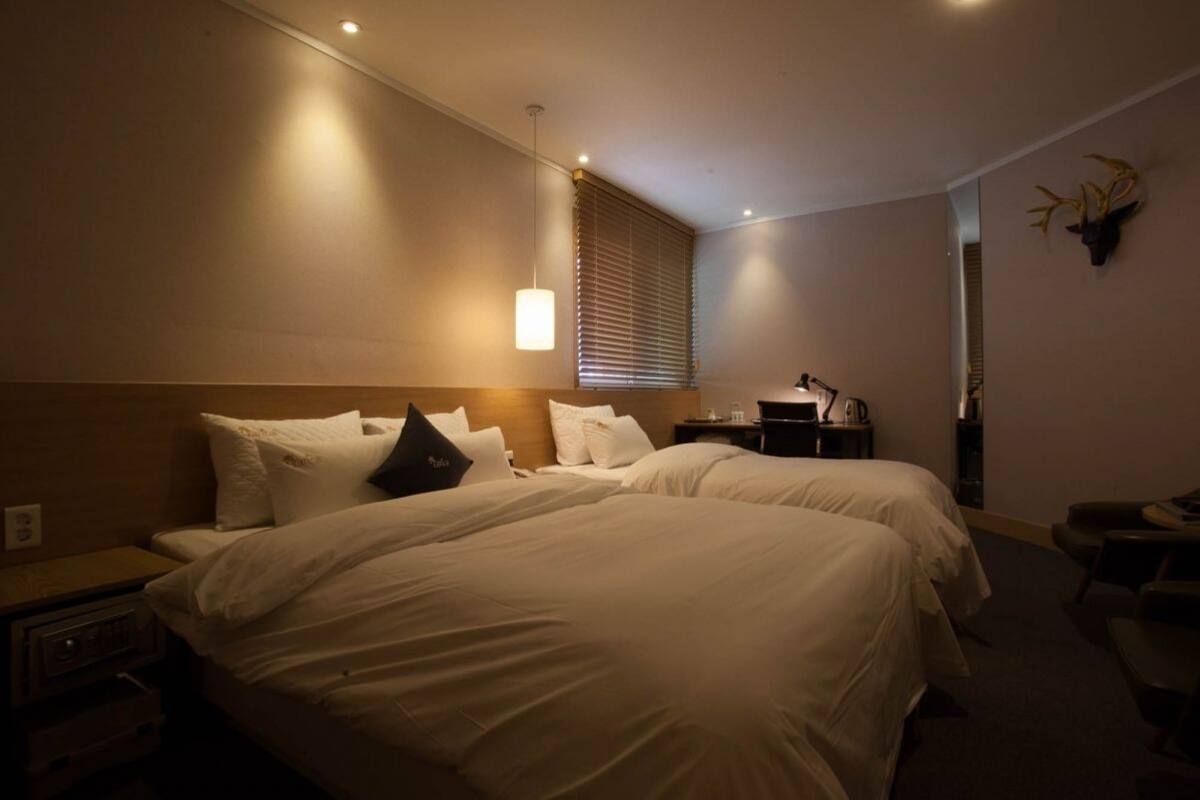 Quarto de hotel com duas camas, uma mesa de cabeceira, uma luminária e uma decoração de cabeça de veado fixada na parede.