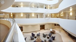 Um hall de hotel em vários níveis, com teto curvo, várias áreas de estar e luminárias esféricas penduradas.