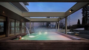 Um spa moderno com uma banheira de hidromassagem em vidro, deck de madeira e vista para a paisagem ao redor.