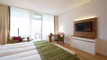 Quarto de hotel com cama grande, escrivaninha, cadeira, televisão e vista para o exterior.
