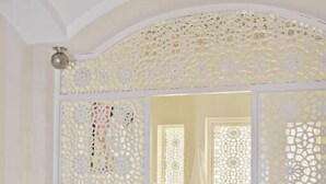 Quarto com cama, cabeceira branca e divisória decorativa branca com desenhos elaborados.