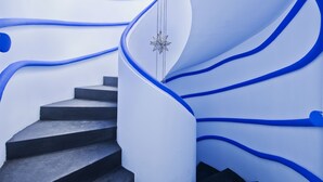 Escadaria em espiral com paredes brancas e detalhes azuis, com um enfeite em formato de estrela pendurado.