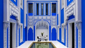 Decoração azul e branca com piscina, cadeiras brancas e uma mesa com um vaso de flores.