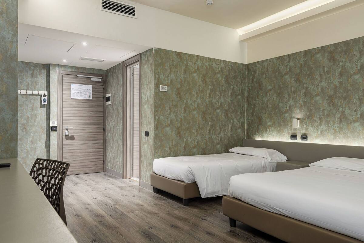 Quarto de hotel com duas camas, uma escrivaninha e uma cadeira.