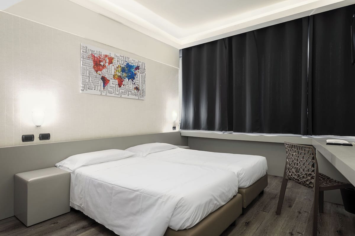 Quarto de hotel com duas camas, um mapa na parede, uma mesa e uma cadeira.