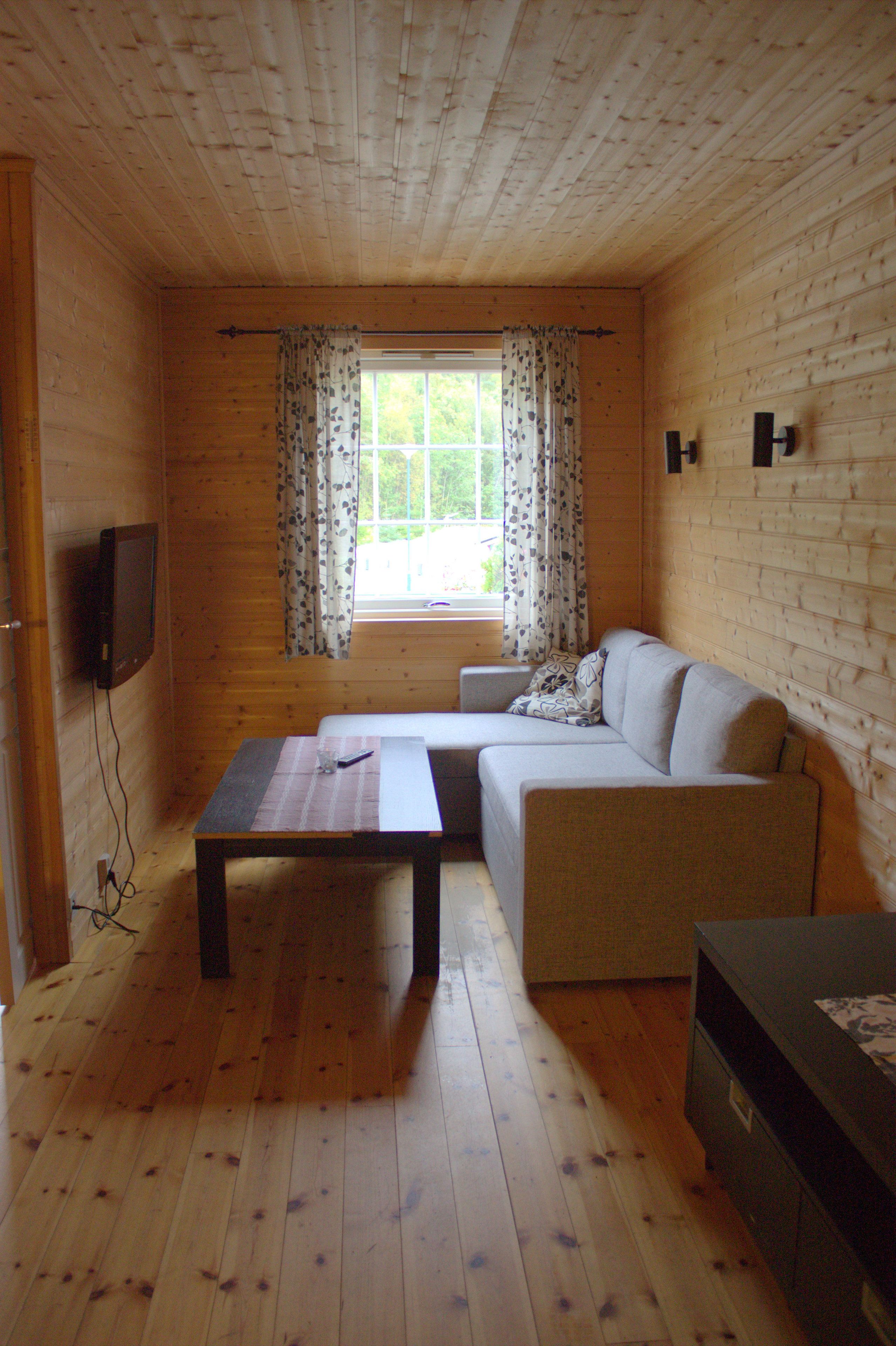 Quarto de cabana de madeira com sofá, mesa, televisão e janela com cortinas.