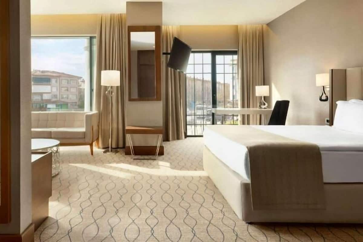 Quarto de hotel com cama grande, escrivaninha, cadeira, televisão e vista da cidade.