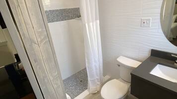 Casa de banho com chuveiro, sanita e lavatório.