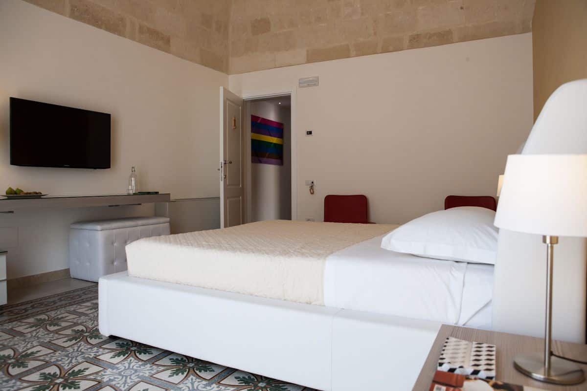 Quarto de hotel com cama, televisão, escrivaninha e porta que dá para outro aposento.