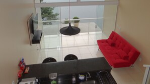Uma sala de estar moderna com um sofá vermelho, uma luminária pendente preta e vista para um lago através de grandes janelas.