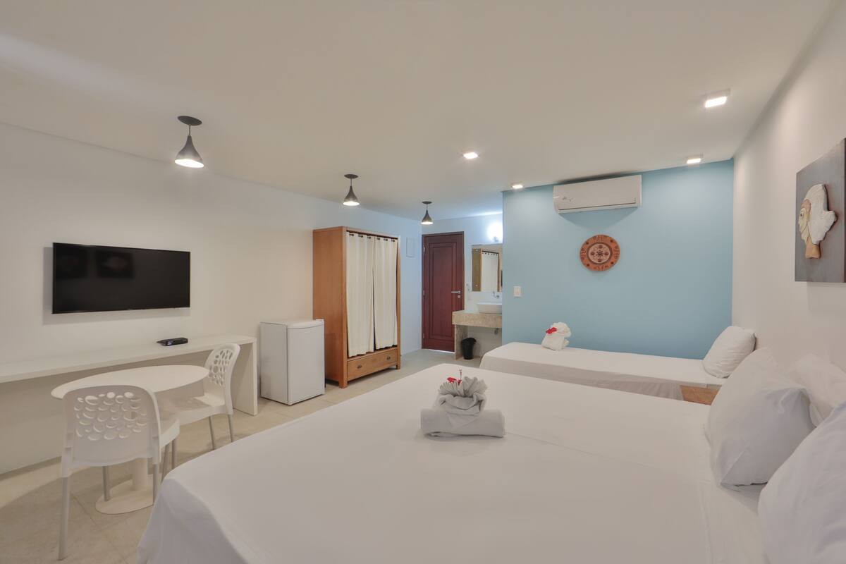Quarto de hotel moderno com uma cama, escrivaninha, cadeira, televisão, espelho e banheiro.