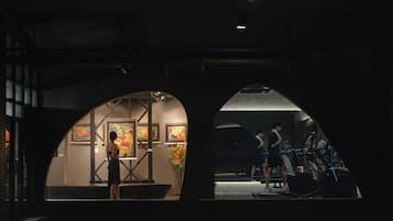 Uma galeria de arte com pinturas expostas e uma área de ginásio com esteiras.