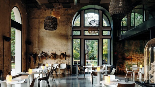 Um restaurante com janelas altas em arco, luminárias pendentes e decoração rústica.