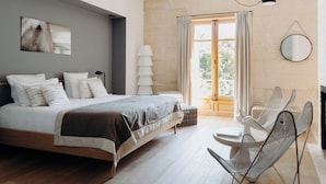 Quarto com uma cama grande, uma mesa de cabeceira, uma cadeira, um abajur e uma janela com cortinas.