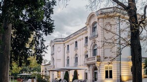 Um edifício imponente com arquitetura clássica, apresentando um pátio amplo com área de estar externa e um jardim bem cuidado.