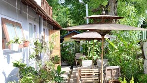 Uma área de pátio com mobiliário externo, plantas em vasos e um edifício com varanda.