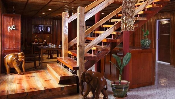 Uma escadaria de madeira com design rústico, uma mesa de madeira com cadeiras e uma estátua decorativa de elefante.