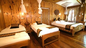 Quarto com paredes e pisos de madeira, duas camas com roupa de cama branca, um banco de madeira e um objeto decorativo na parede.