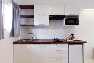 Uma cozinha moderna com armários brancos, uma pia de aço inoxidável, micro-ondas e uma geladeira compacta.