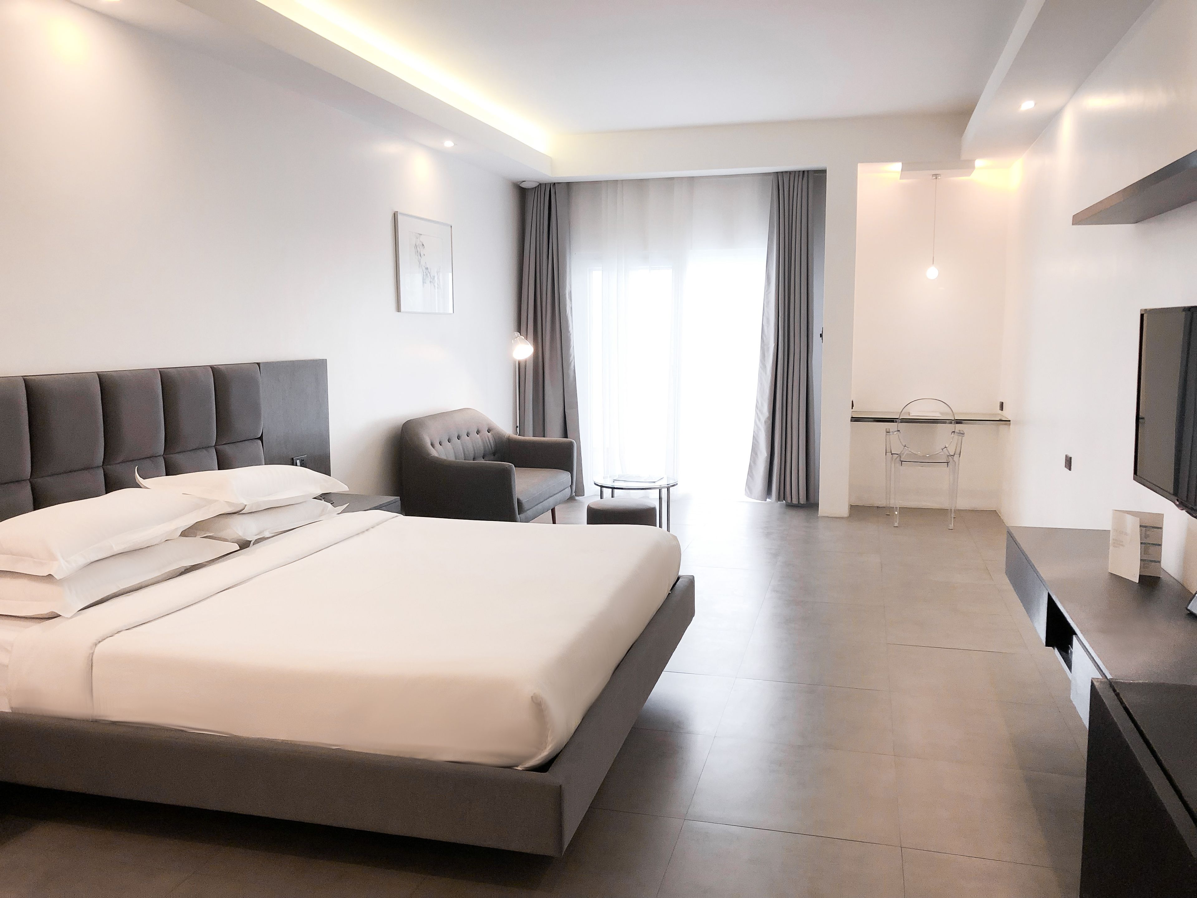 Quarto de hotel moderno com uma cama grande, uma escrivaninha, uma cadeira e uma televisão.