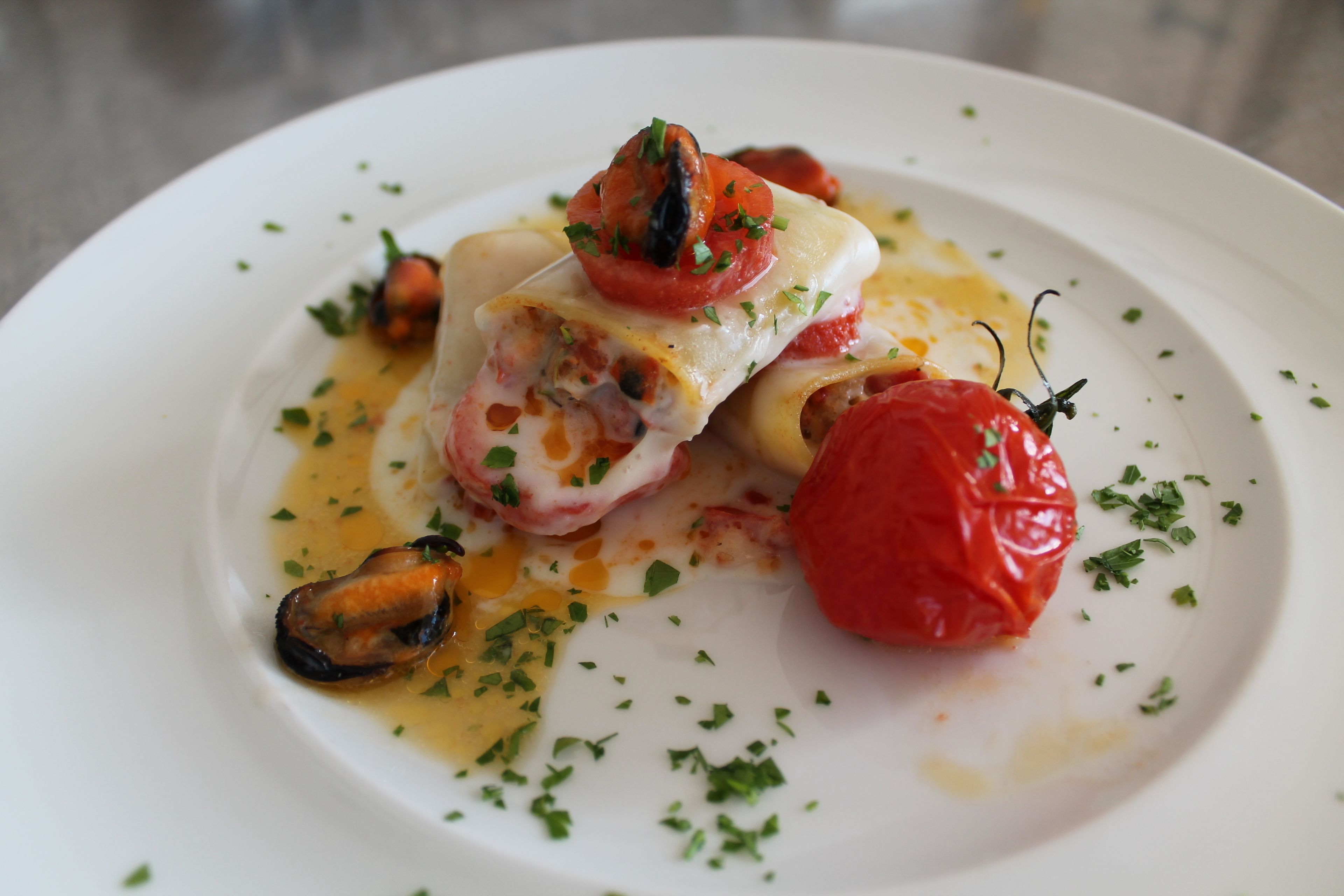 Um prato branco com filé de peixe, tomate cereja e mexilhões.