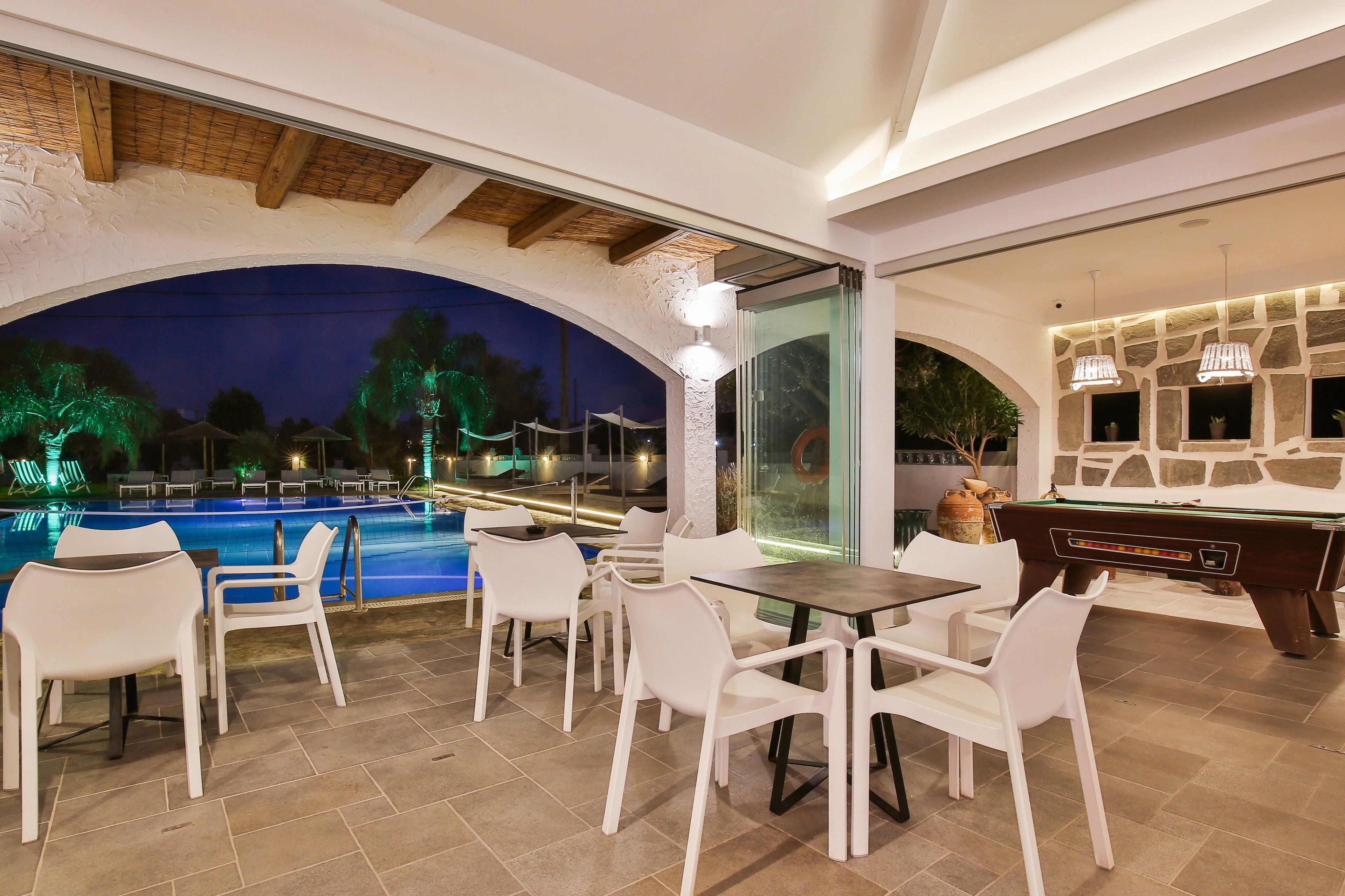 Espaço interno da piscina com vista para o céu noturno, mesa de bilhar e cadeiras brancas.