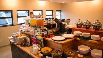 Buffet com diversos alimentos e bebidas, incluindo uma grande tigela de ponche e vários dispensadores de café.