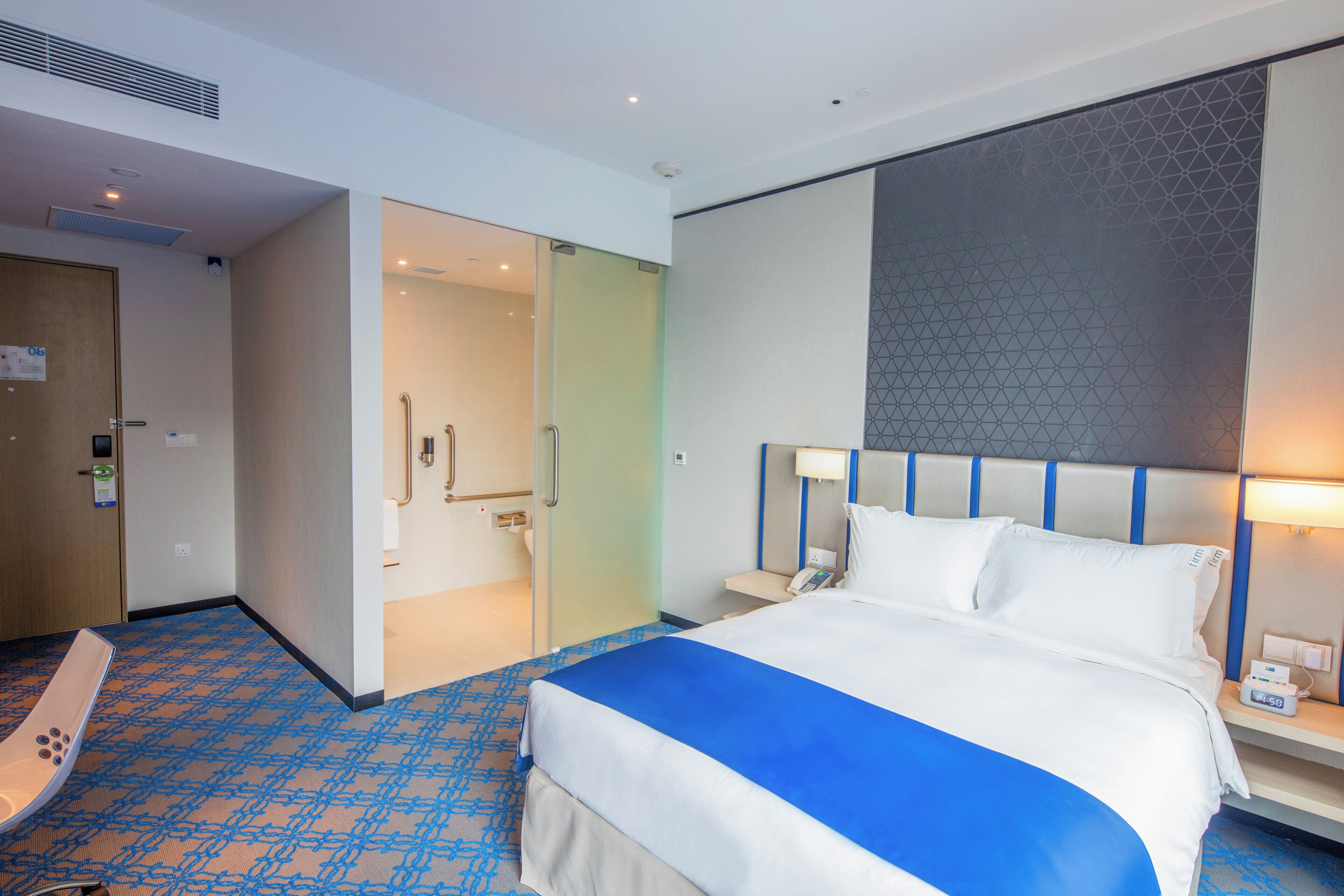 Quarto de hotel com cama, mesa de cabeceira e banheiro com chuveiro.