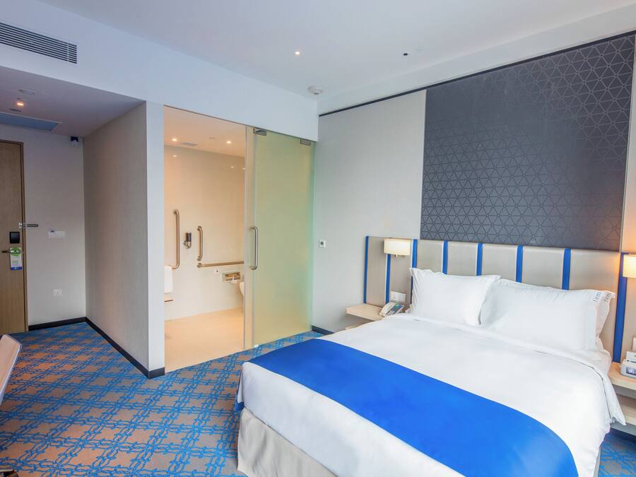 Quarto de hotel com cama, mesa de cabeceira e banheiro com chuveiro.