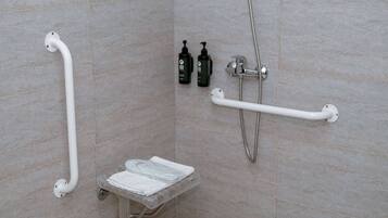Um banheiro com chuveiro, barras de apoio, um pequeno banco e duas garrafas de shampoo.