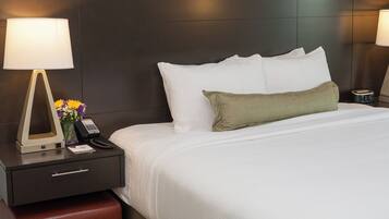 Quarto de hotel com cama, mesa de cabeceira, abajur, telefone e relógio.