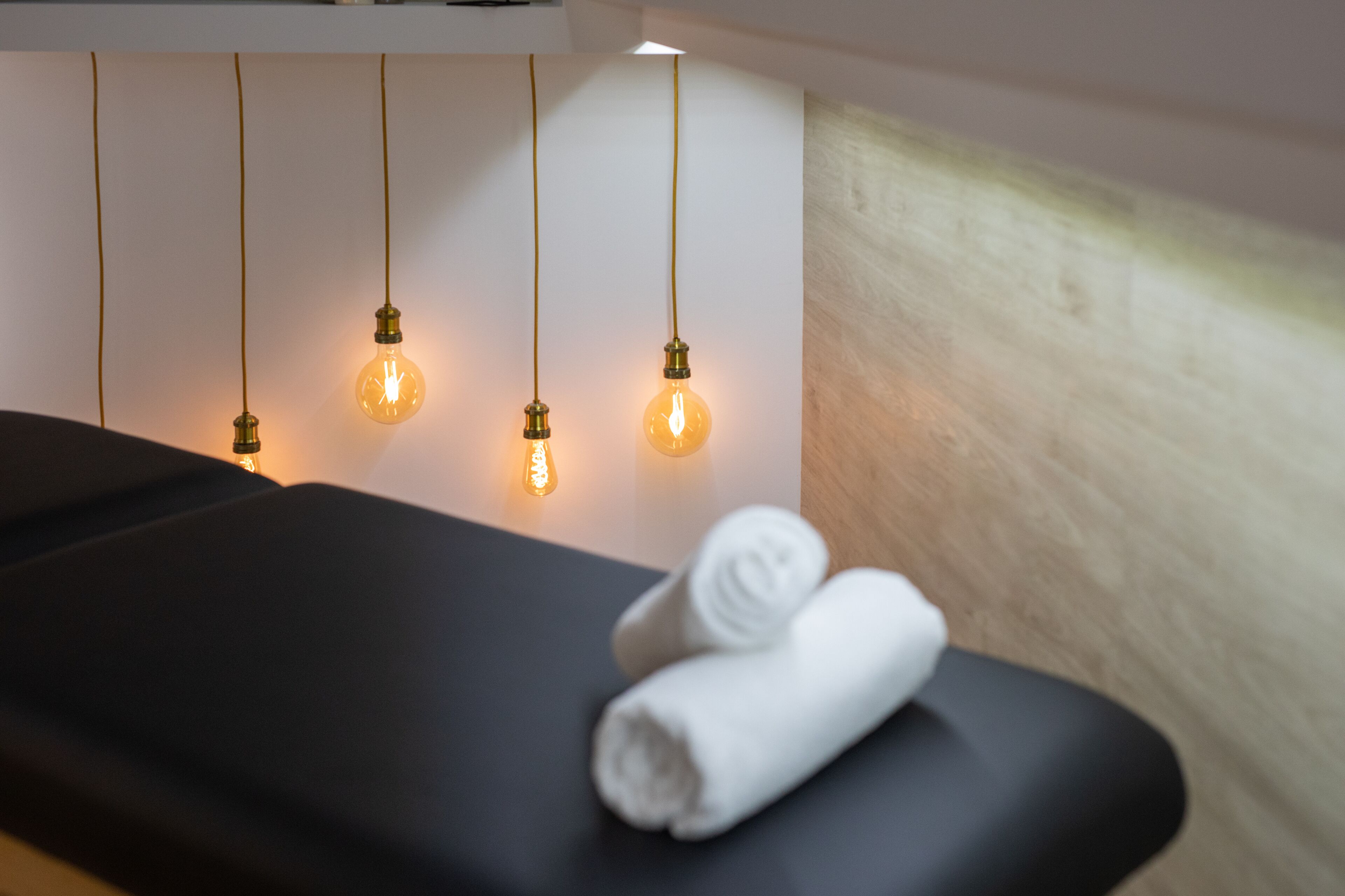 Mesa de massagem com toalhas enroladas e lâmpadas penduradas.