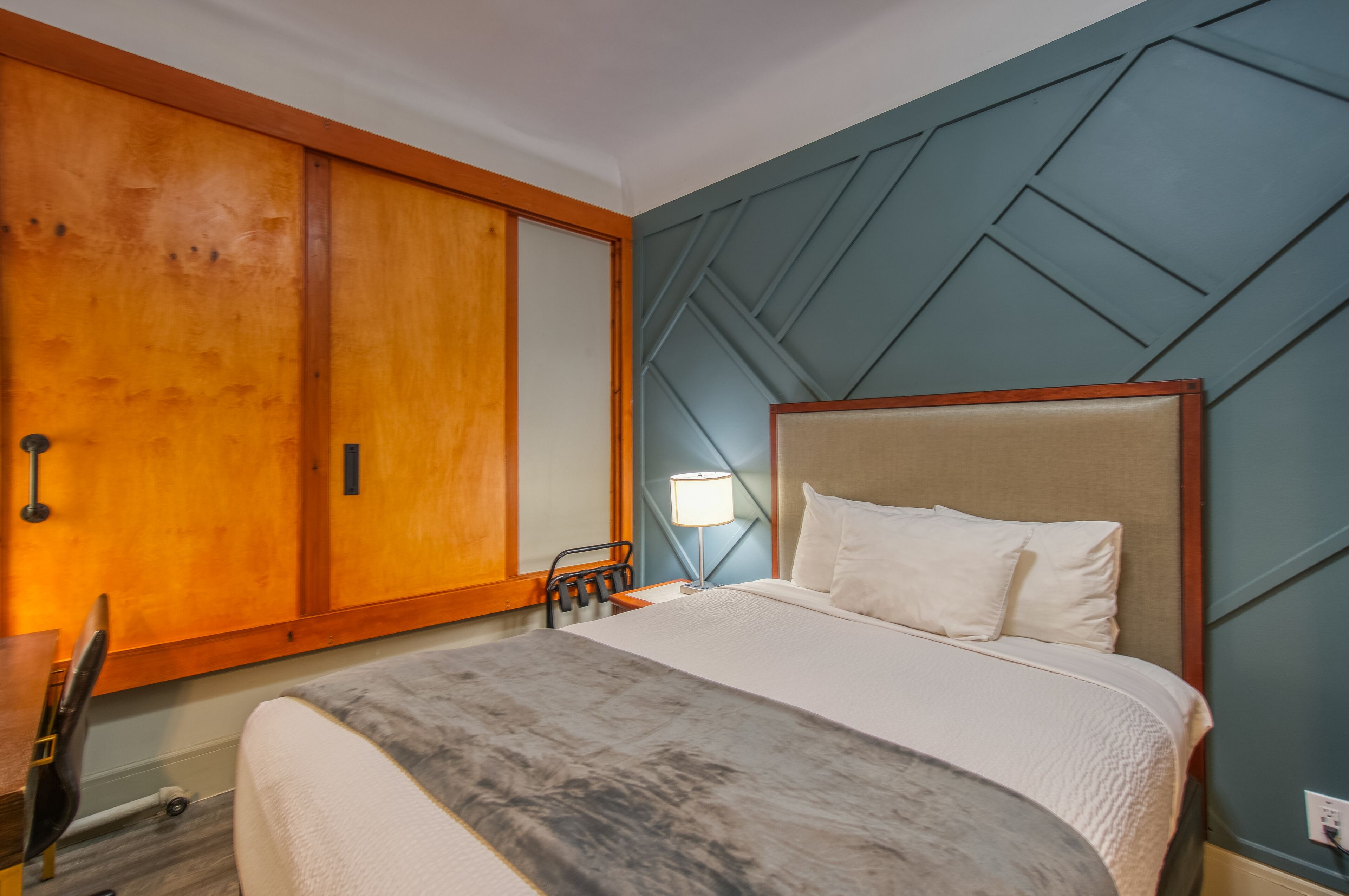 Quarto de hotel com cama, armário de madeira e parede com padrões geométricos.