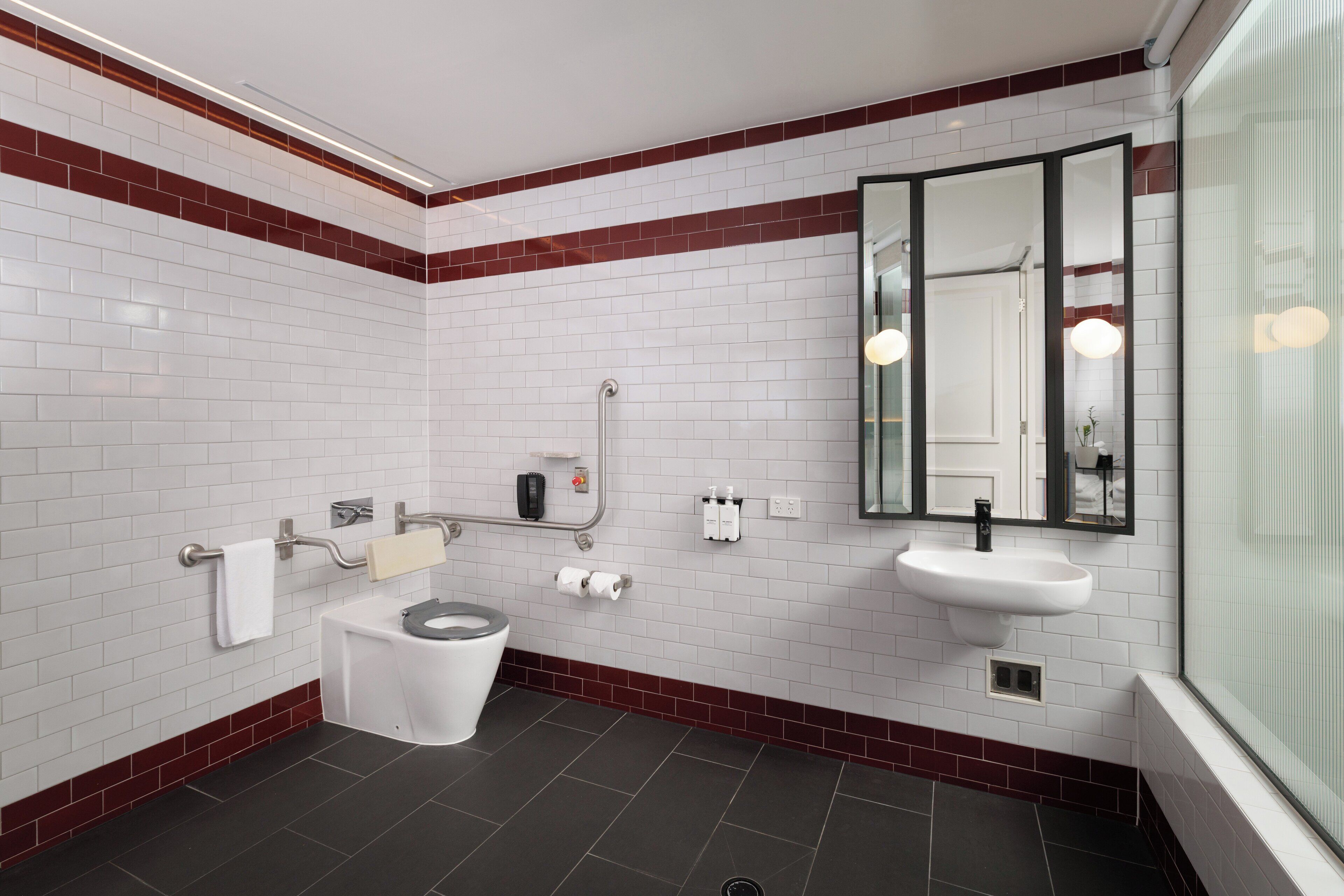 Um banheiro moderno com azulejos brancos tipo metrô, uma parede de destaque com azulejos vermelhos, vaso sanitário branco, pia com espelho e box de vidro.