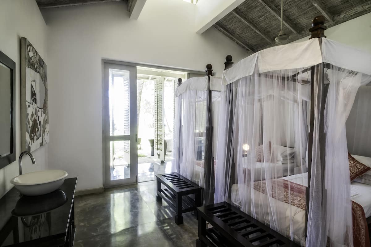 Quarto com cama de dossel, mesa de cabeceira, um banco e banheiro com pia e espelho.