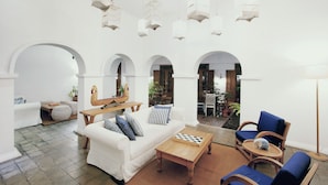 Ampla sala de estar com sofá branco, mesa de centro de madeira e poltronas azuis acolchoadas.