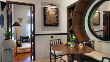 Uma área de refeições com uma mesa redonda, cadeiras e um banco. Há uma obra de arte na parede e um espelho decorativo.