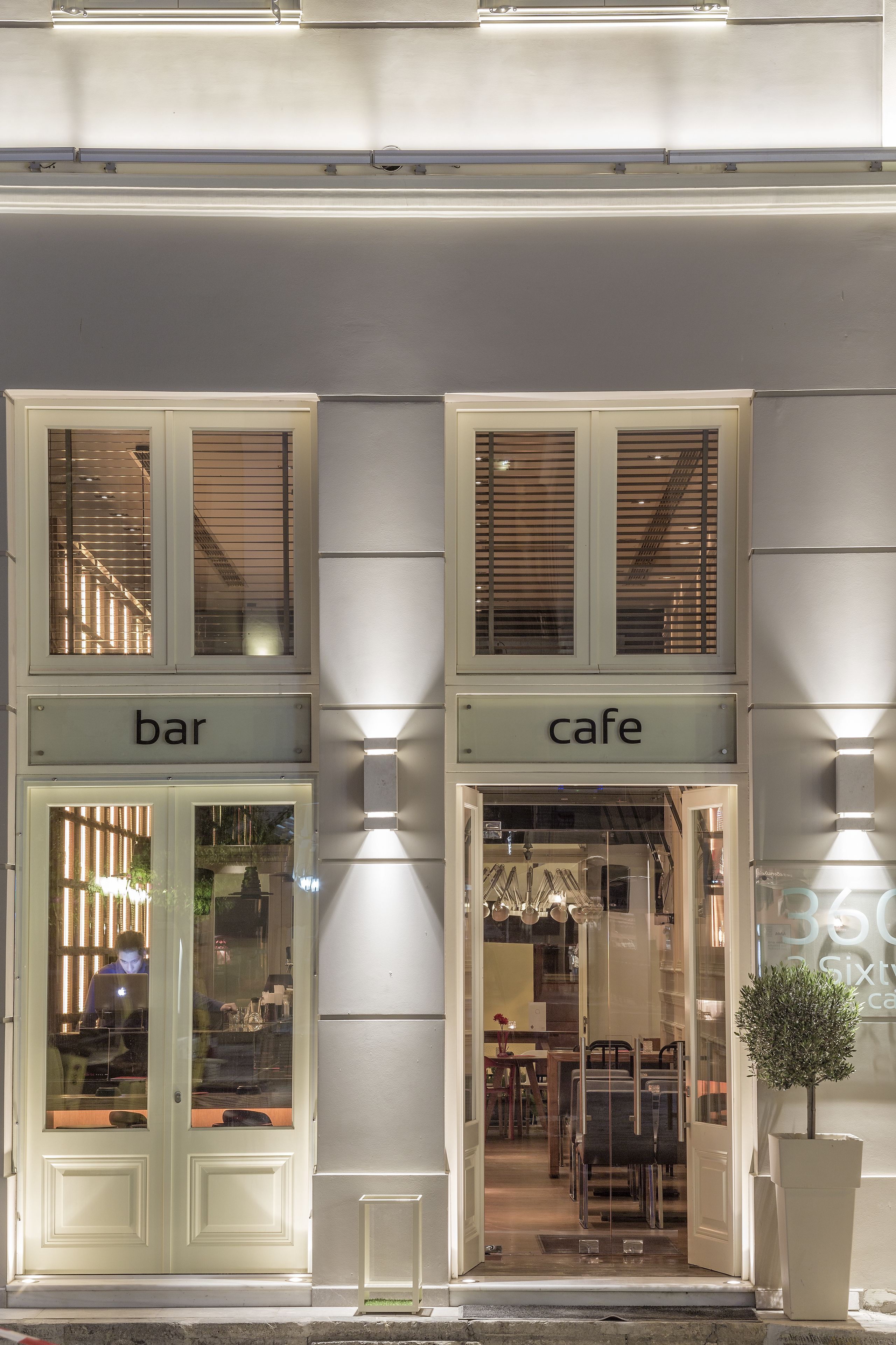 Edifício com bar e entrada de café, com portas de vidro e uma planta em vaso na frente.