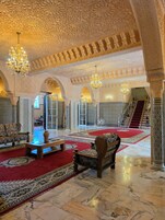 Um interior ricamente decorado com uma escadaria imponente, lustres e carpetes estampados.