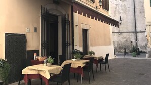 Um café ao ar livre com mesas e cadeiras, um edifício com relógio e uma rua de calçada.