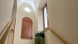 Uma escada com uma porta de madeira no topo, um vaso de planta e uma pequena janela na parede.