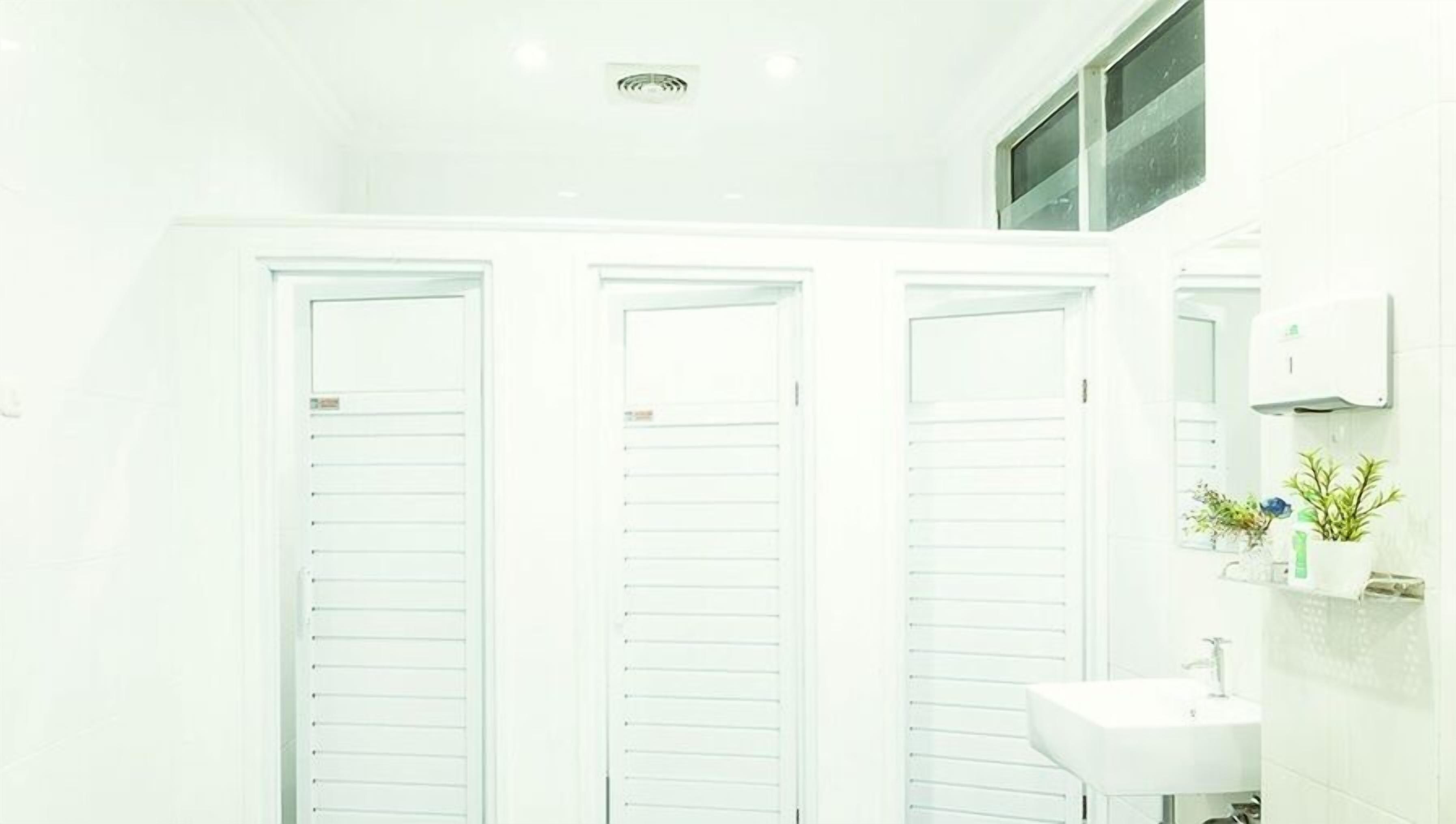Um banheiro claro e branco com três portas, uma pia e um espelho.
