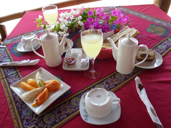 Mesa posta com diversas opções de café da manhã, incluindo pão, geleia e frutas, além de vários bules e xícaras de chá brancas.