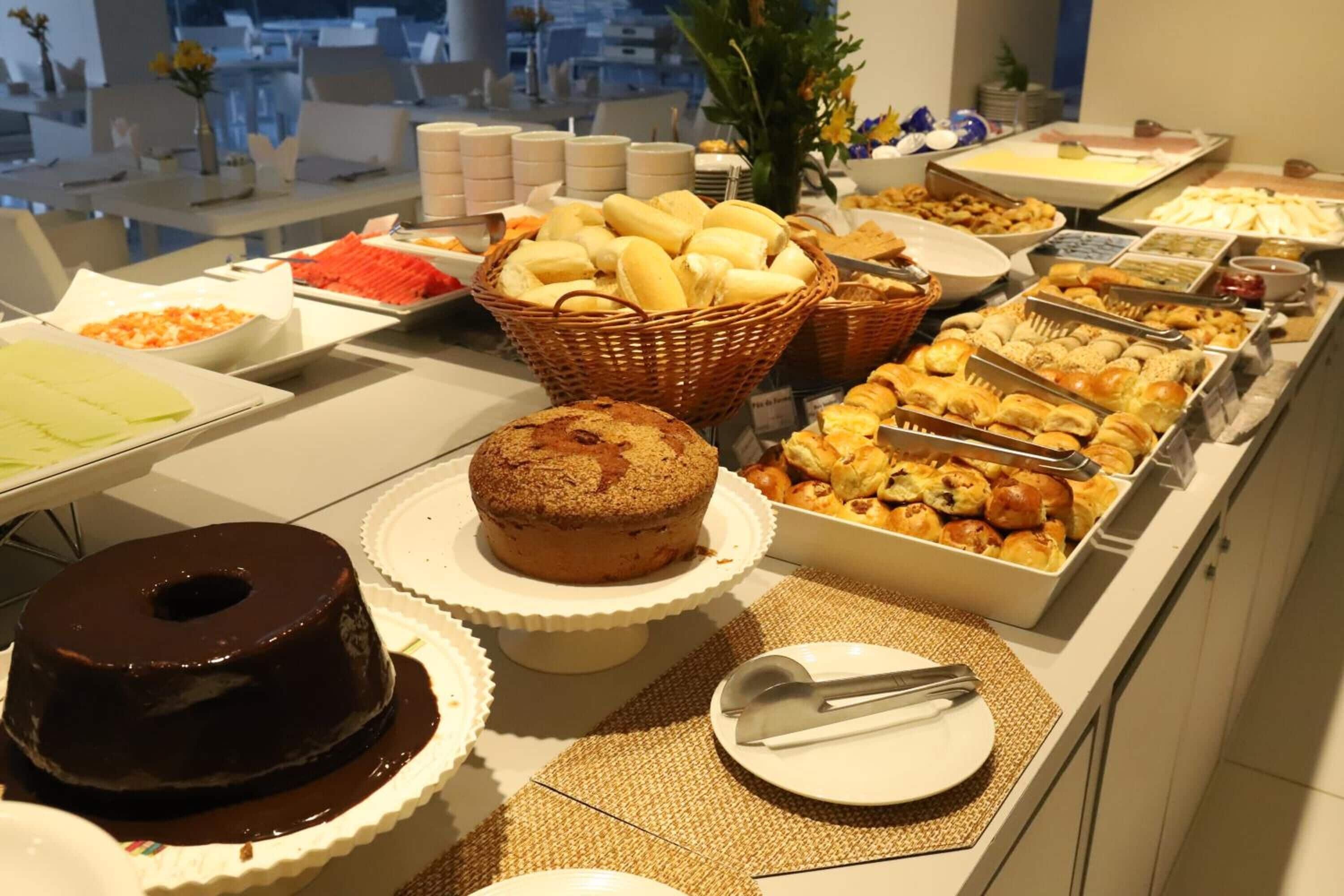 Buffet com diversos alimentos, incluindo bolo de chocolate, pão e doces.