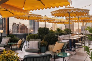 Terraço no telhado com área de estar externa, guarda-sóis amarelos e vista para a cidade.