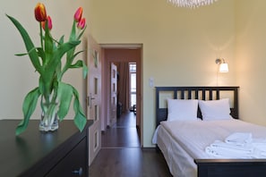 Quarto de hotel com uma cama, mesa de cabeceira com um vaso de tulipas, criado-mudo e uma luminária fixada na parede.