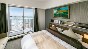 Quarto de hotel com uma cama grande, vista da cidade através de uma varanda e uma pintura na parede.