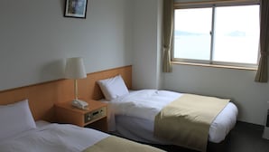 Quarto de hotel com duas camas, uma mesa de cabeceira com abajur, telefone e janela com cortinas.