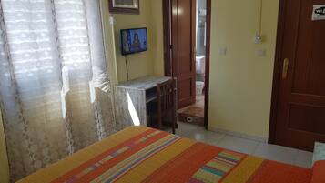 Quarto com cama, escrivaninha de madeira, televisão e guarda-roupa.