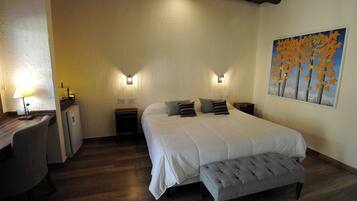 Quarto com cama, mesas de cabeceira, escrivaninha, luminária e um quadro na parede.